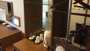 Quarto de hotel com escrivaninha de madeira, prateleira de vidro, espelho e área de duche.