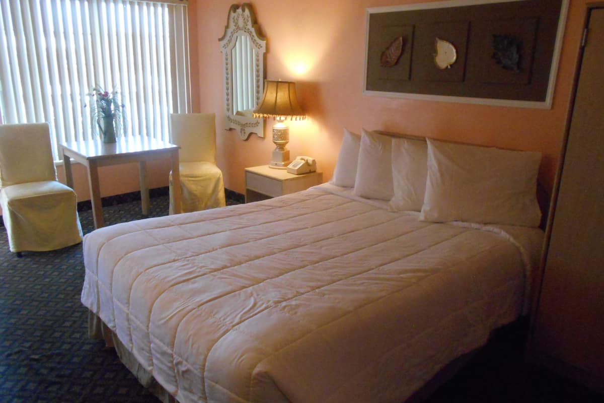 Quarto de hotel com uma cama grande, uma escrivaninha, uma cadeira, um abajur e um quadro na parede.