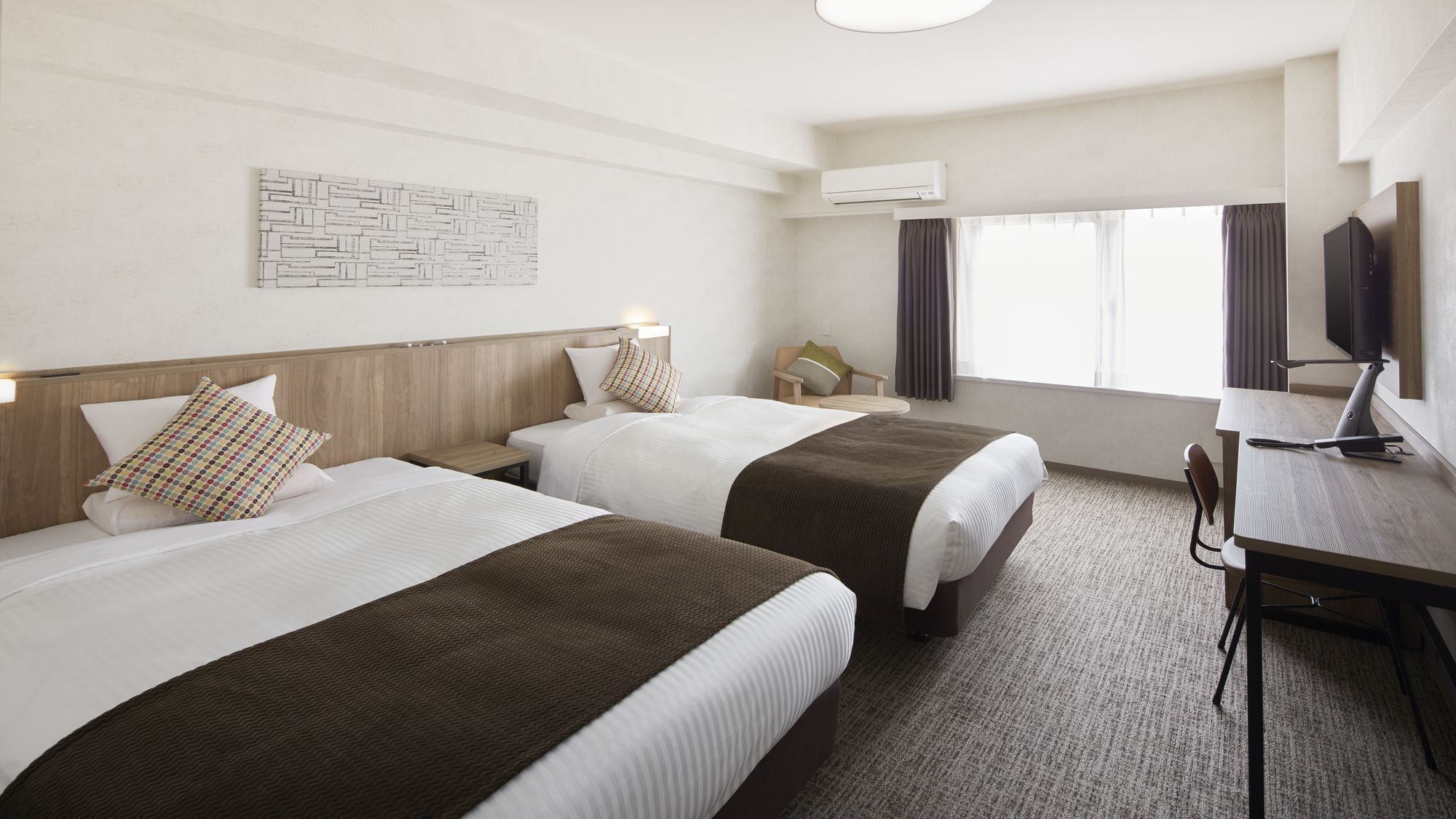 Quarto de hotel com duas camas, uma escrivaninha com cadeira, televisão e ar condicionado.