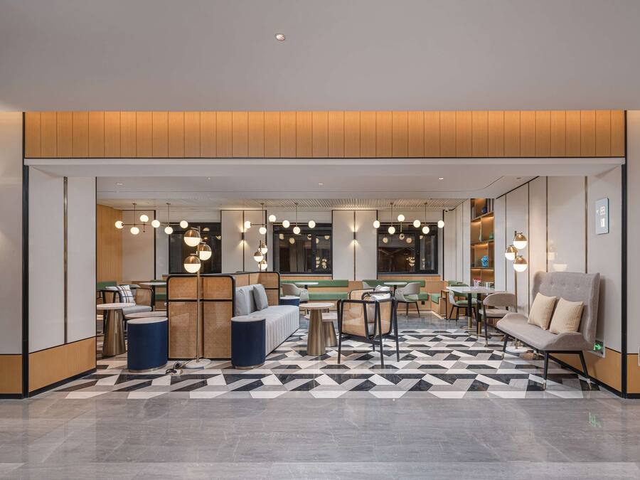 Um lobby moderno com piso estampado em padrão geométrico, áreas de estar e iluminação pendente.