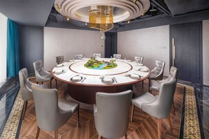 Sala de conferência com mesa redonda, cadeiras estofadas cinzas e um objeto decorativo no centro.