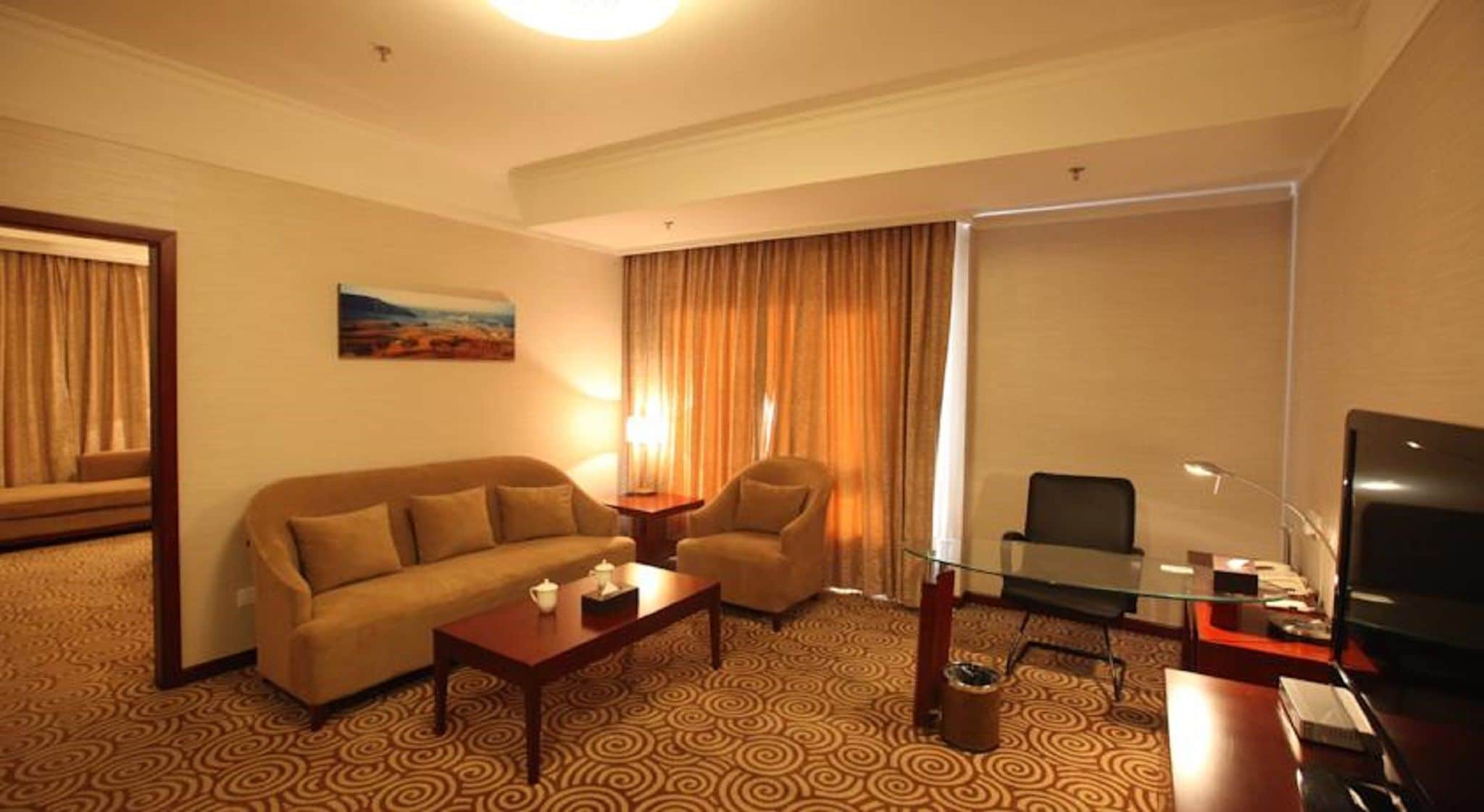 Quarto de hotel com sofá, poltrona, mesa de centro, televisão e um quadro na parede.