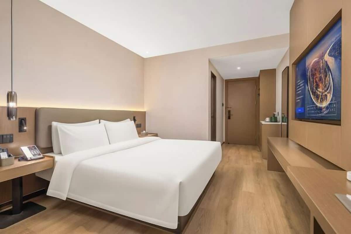 Quarto de hotel moderno com uma cama grande, mesas de cabeceira, uma escrivaninha e televisão na parede.