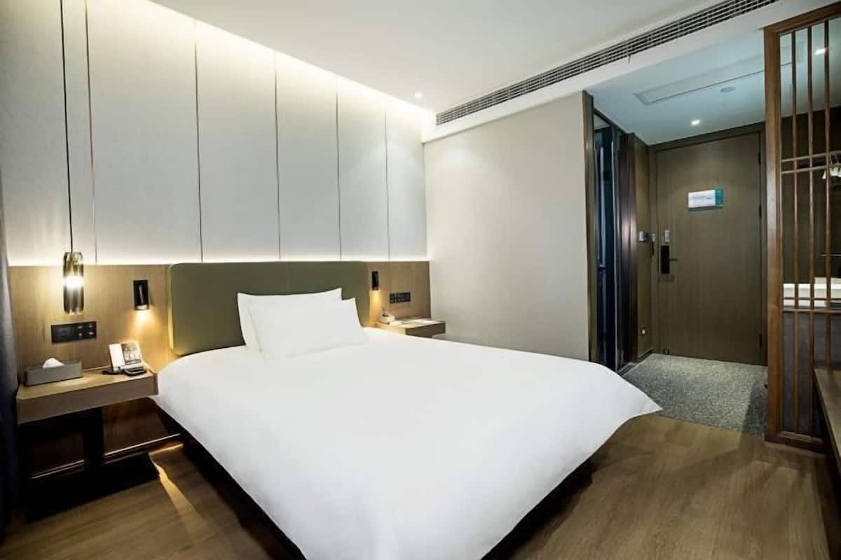 Quarto de hotel com uma cama grande, mesas de cabeceira, um criado-mudo, cabeceira de madeira e uma porta com portão de segurança.