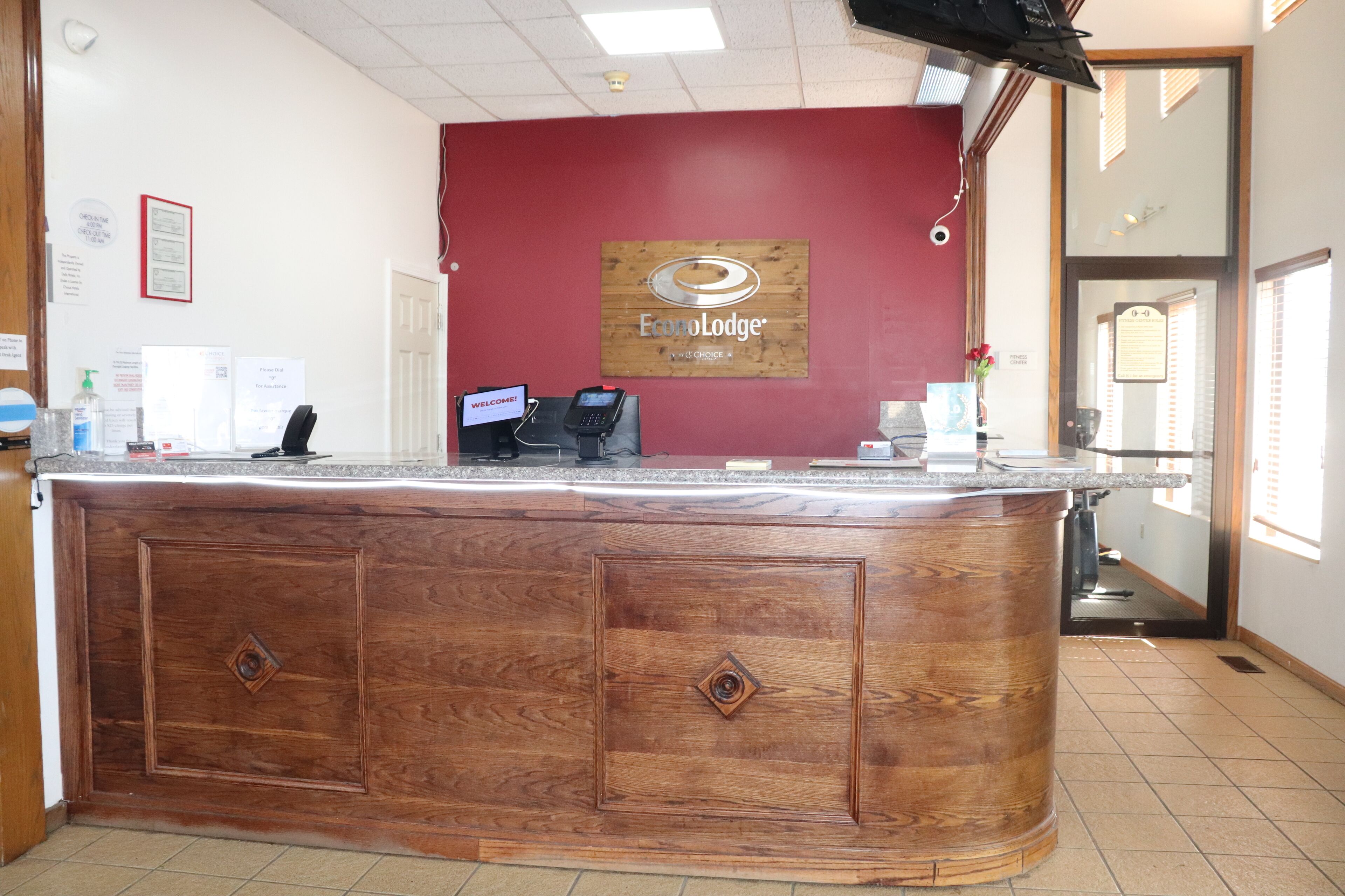 Uma receção com acabamento em madeira, uma parede vermelha com o logótipo 'EconoLodge' e um letreiro de 'Welcome'.