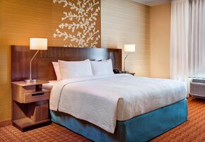 Quarto de hotel com uma cama grande, duas mesas de cabeceira com abajures, um painel decorativo na parede e um aparelho de ar condicionado.