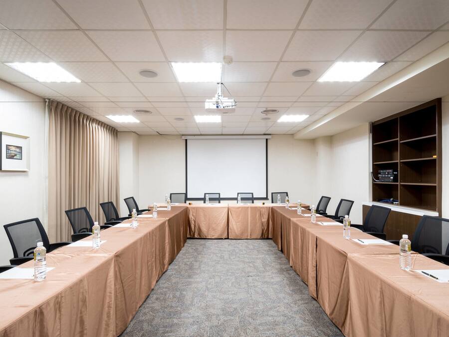 Uma sala de conferências com uma mesa comprida, cadeiras, uma tela de projetor e uma estante.