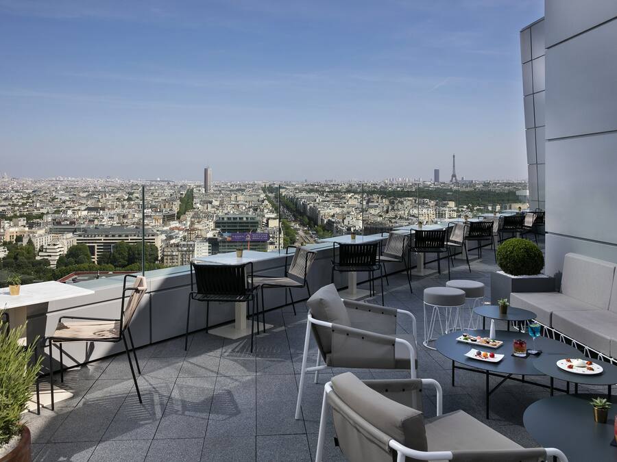 Terraço no telhado com área de estar externa, vista da cidade e fachada de um edifício moderno.