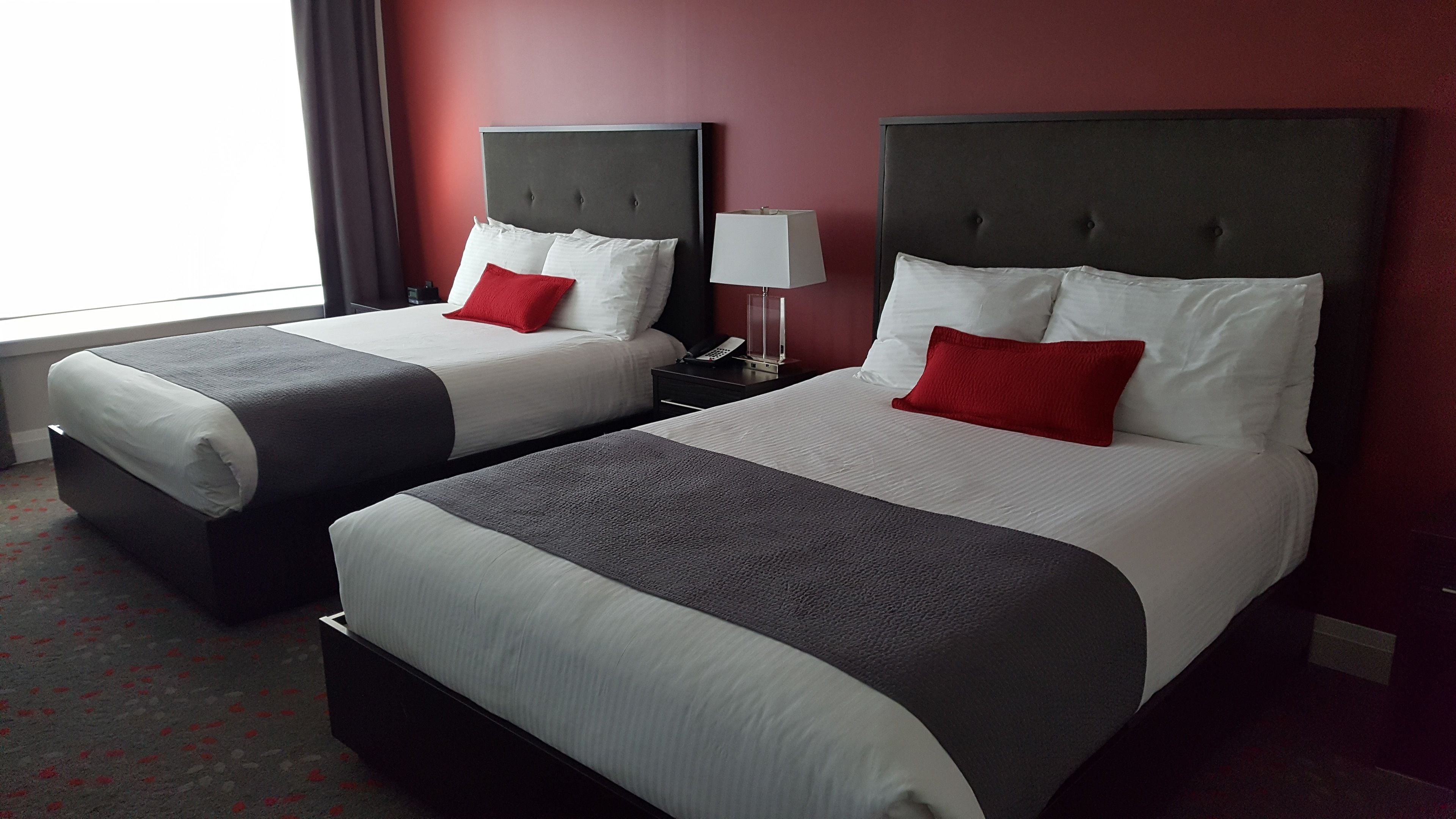 Duas camas de solteiro com roupa de cama cinza e branca, almofadas vermelhas e uma mesa de cabeceira com abajur entre elas.