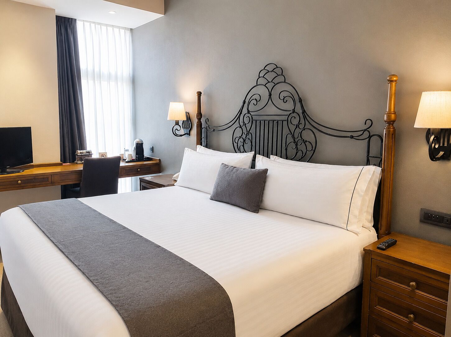 Quarto de hotel com uma cama grande, uma escrivaninha com cadeira, televisão e janela com cortinas.