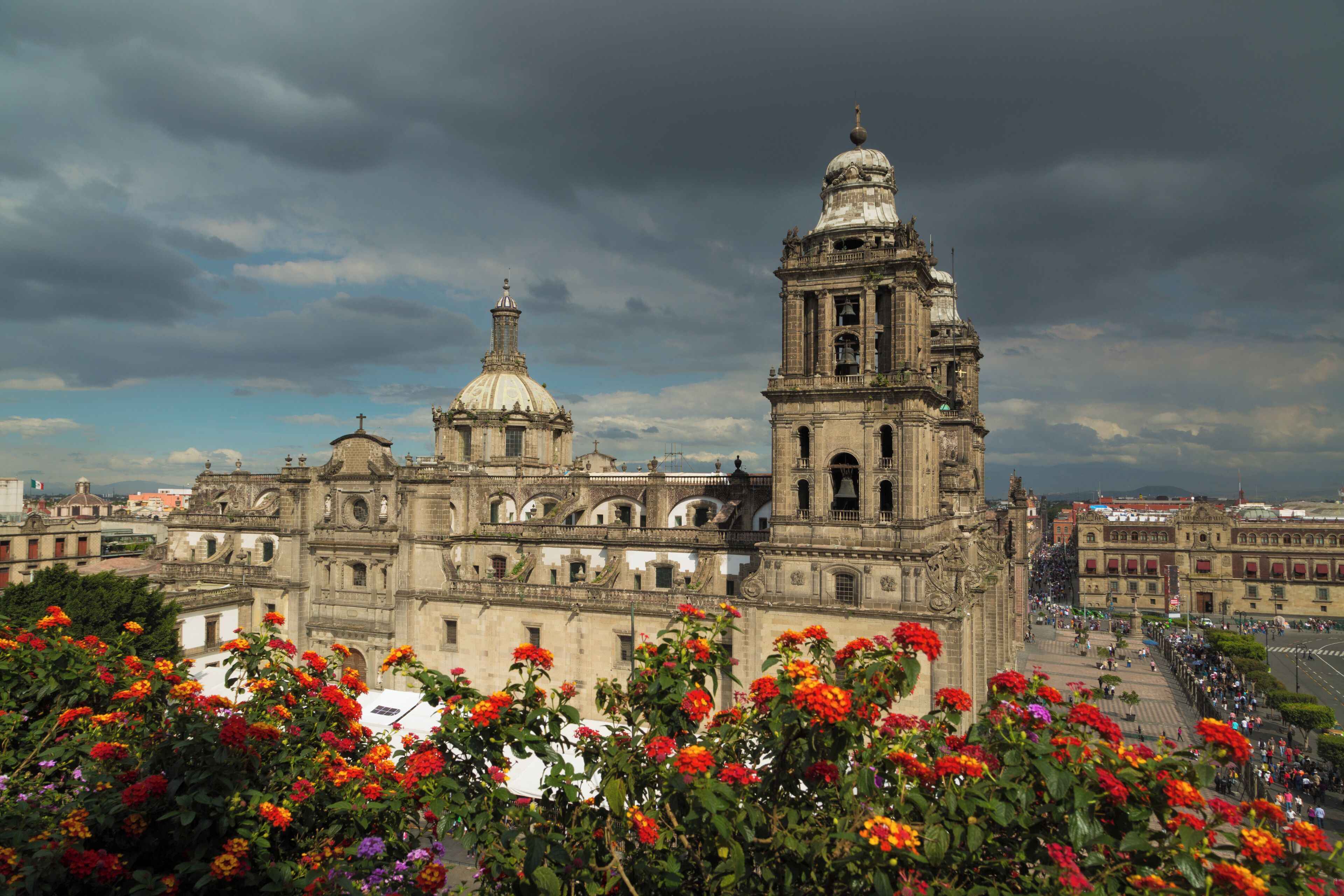 Um edifício histórico com várias cúpulas e um campanário, rodeado por flores coloridas.