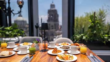 Mesa de jantar com itens de café da manhã e vista para a cidade através de grandes janelas.