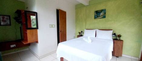 Quarto de hotel com cama, mesa de cabeceira, escrivaninha e parede verde.