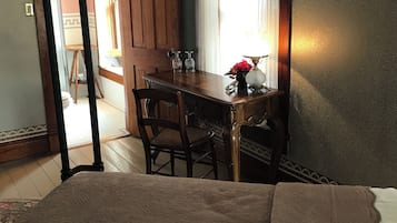 Quarto com cama, escrivaninha de madeira, cadeira e janela com cortinas.