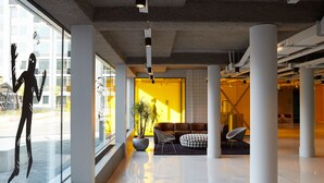 Um lobby moderno com parede de vidro, sofá de couro marrom e um banquinho quadriculado.