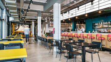Um restaurante moderno com mesas amarelas, cadeiras pretas e um espaço de bar com banquetas vermelhas.