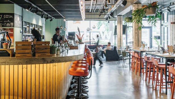 Uma área de bar moderna com balcão curvo, banquetas e um painel de cardápio visível.