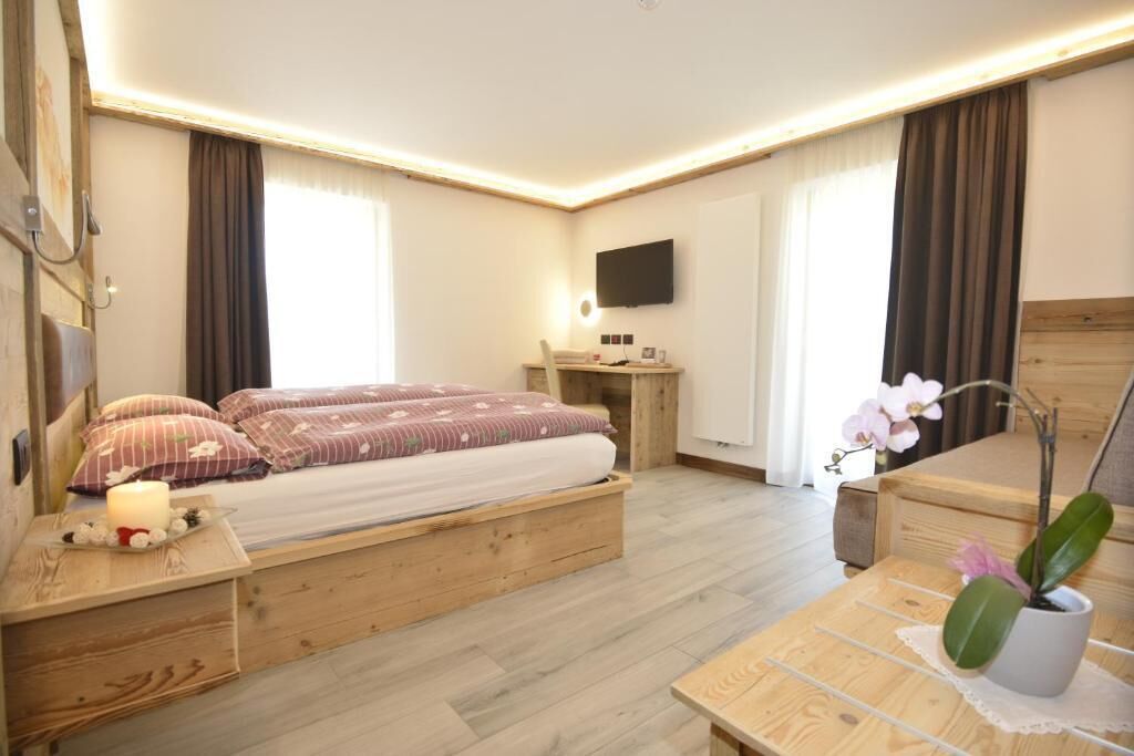 Quarto com cama de madeira, mesa de cabeceira, abajur e pequena escrivaninha com cadeira.