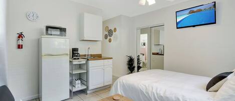 Quarto de hotel moderno com cama, escrivaninha, frigorífico, máquina de café, televisão e ventoinha de teto.