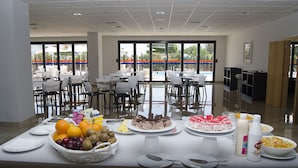 Mesa de buffet com diversos alimentos e vista para área externa com mesas.