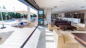 Um lobby moderno de hotel com área de piscina, assentos ao ar livre e uma recepção.