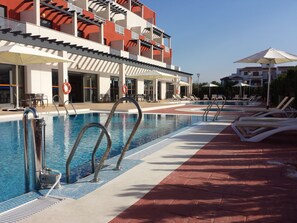 Piscina com grades de metal, espreguiçadeiras e guarda-sóis.