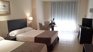 Quarto de hotel com duas camas, uma escrivaninha, uma cadeira, uma televisão e uma janela com cortinas.