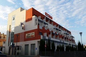 Hotel com design moderno, apresentando esquema de cores vermelho e branco, várias varandas e uma placa indicando que é um hotel 3 estrelas.
