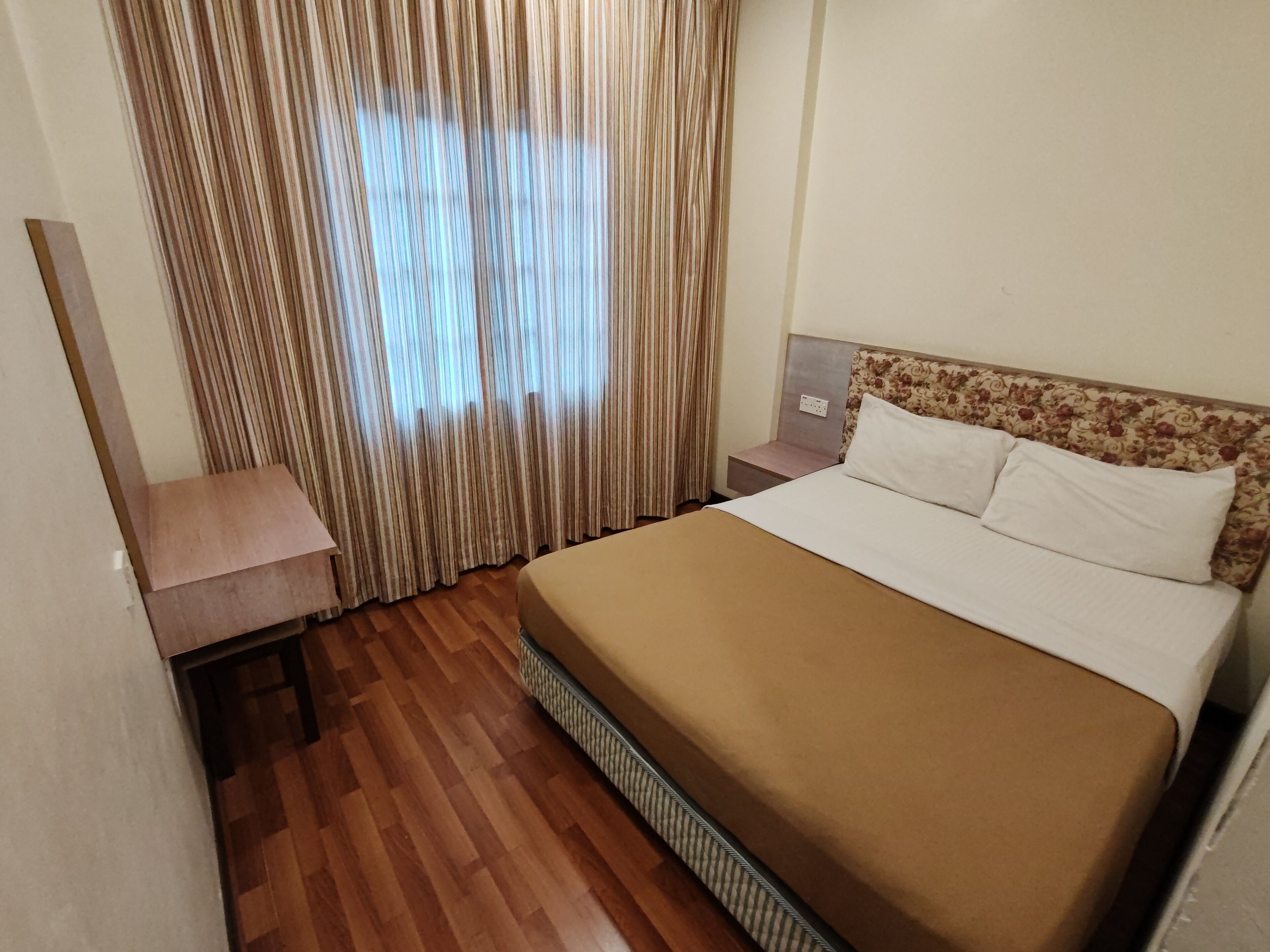 Quarto com cama, mesa de cabeceira, escrivaninha e janela com cortinas.