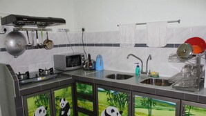 Cozinha equipada com micro-ondas, fogão e utensílios diversos. Armários com tema de panda e pia com escorredor de louça.