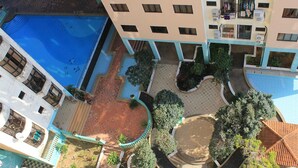 Um edifício de vários andares com um pátio central que inclui uma piscina, rodeado por varandas e vegetação.