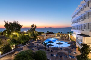 Área de piscina do resort com vista para o mar ao pôr do sol, cercada por espreguiçadeiras e guarda-sóis.