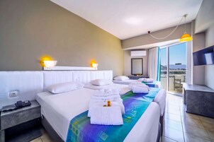 Quarto de hotel com uma cama grande, mesa de cabeceira com telefone, banheiro com espelho e televisão na parede.