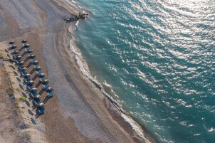 Vista aérea de uma praia com fileiras de guarda-sóis e espreguiçadeiras ao longo da costa.