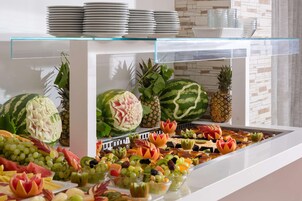 Buffet com diversas frutas e vegetais, incluindo melancia e abacaxi, expostos em um balcão de vidro.