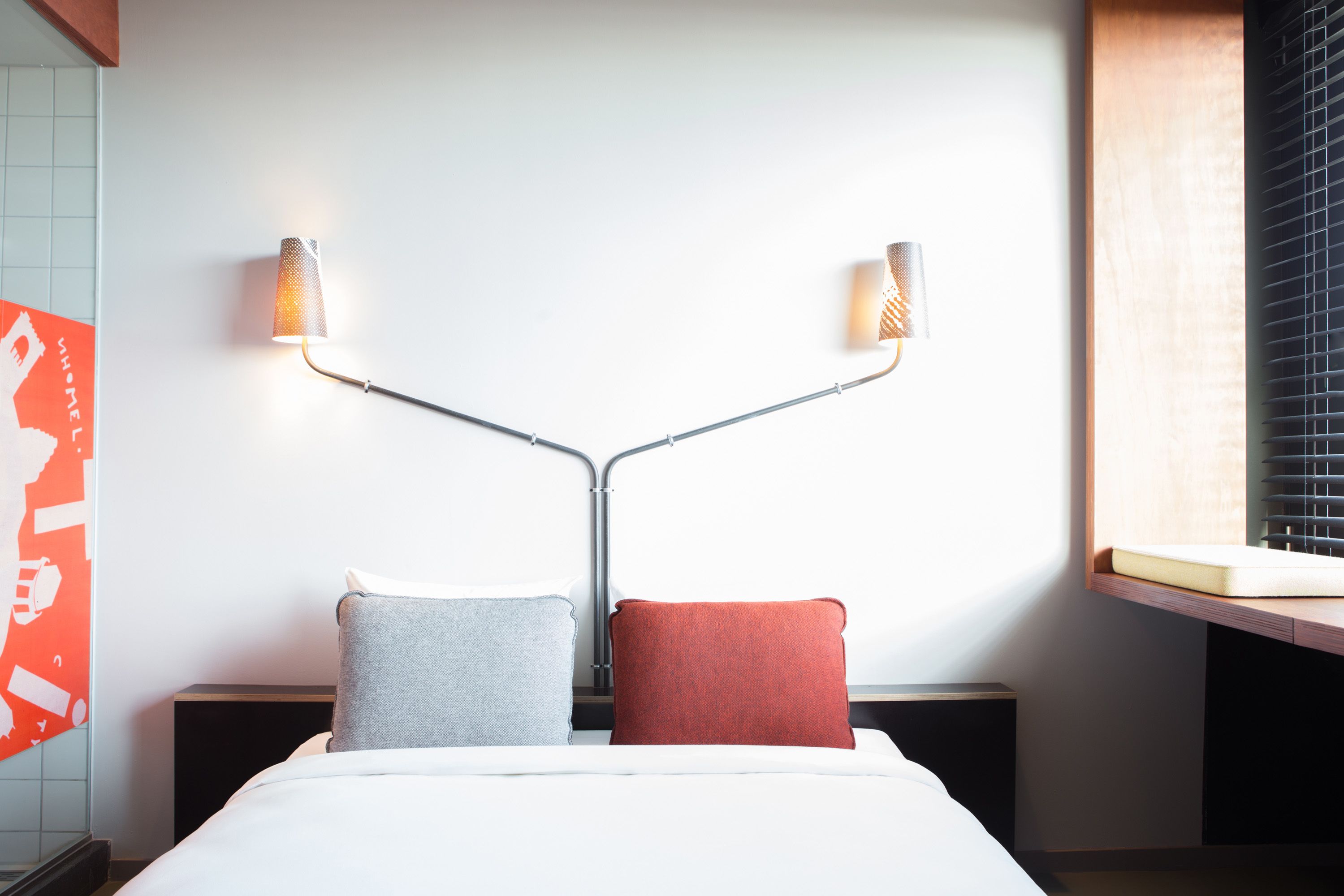 Quarto de hotel moderno com cama, duas luminárias na parede e janela com persianas.