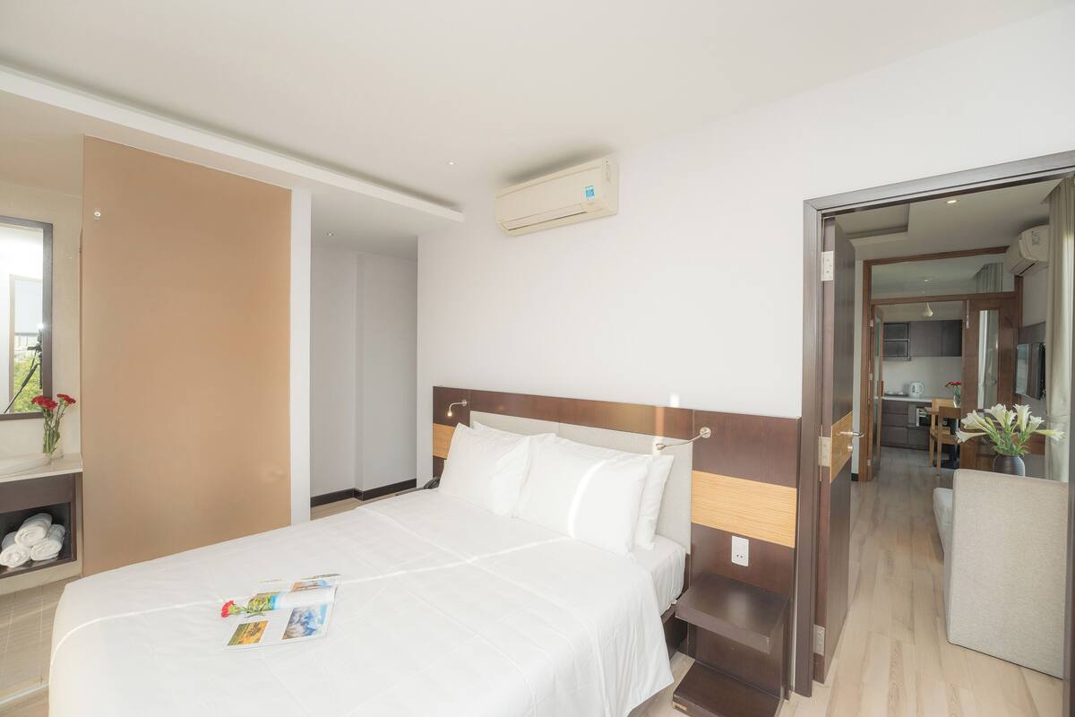 Quarto de hotel com cama, mesa de cabeceira, ar condicionado fixado na parede e vista para a área da cozinha.