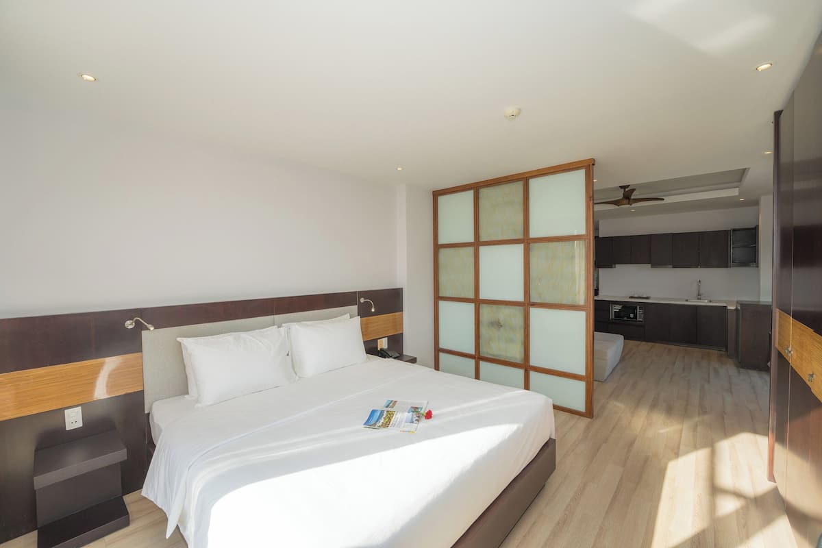 Quarto de hotel com uma cama grande, cabeceira de madeira, mesa de cabeceira, prateleira embutida, porta de vidro deslizante para a cozinha e um ventilador de teto.