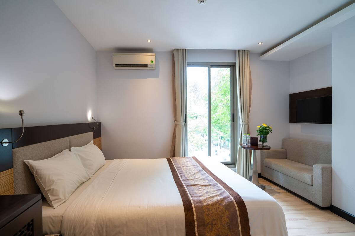 Quarto de hotel com cama, televisão, sofá e janela com cortinas.