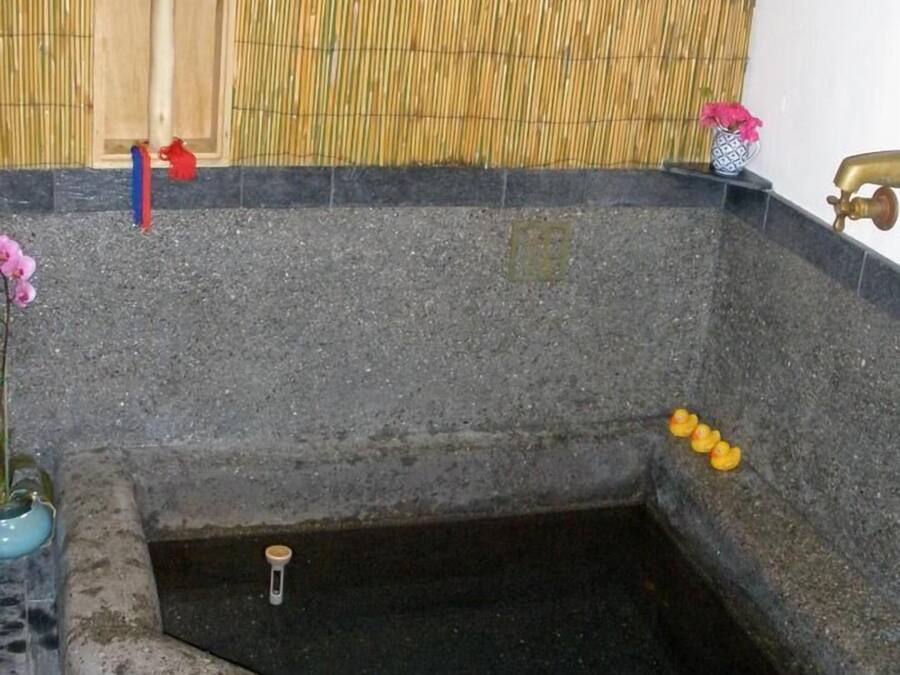 Uma banheira de hidromassagem com um fundo de bambu, um banquinho de madeira e um termômetro pequeno.