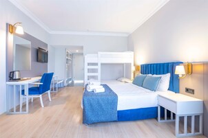 Quarto de hotel com uma cama de beliche, uma escrivaninha com cadeira, mesa de cabeceira e luminária.