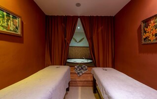 Quarto com duas camas, uma janela grande com cortinas, piso de madeira e um quadro na parede.