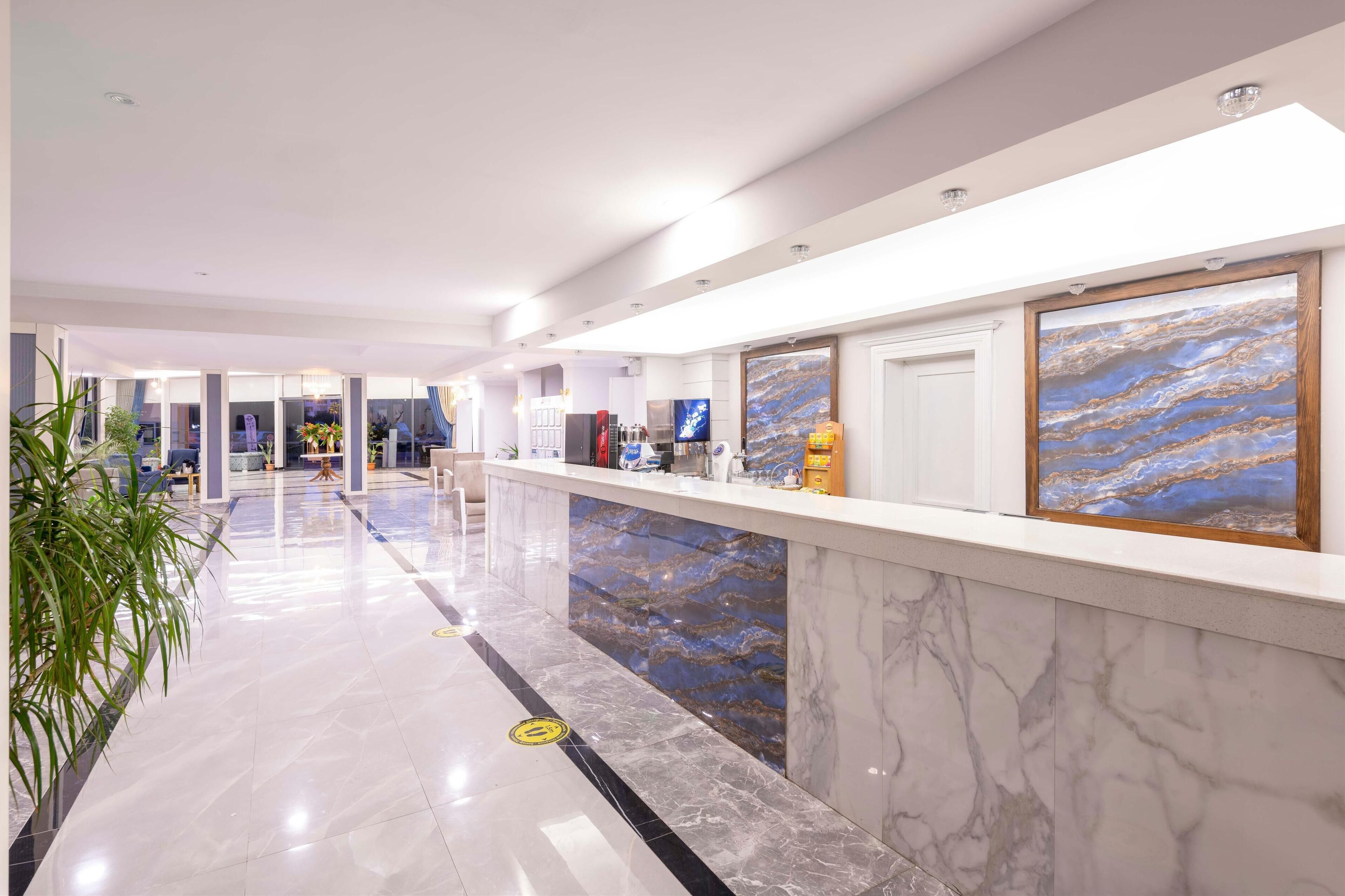 Uma área de recepção de hotel com piso de mármore, balcão de recepção, uma pintura grande e um vaso de plantas.