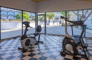 Uma academia com duas bicicletas ergométricas e uma esteira, janelas amplas com vista para a área externa.