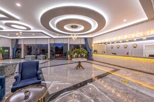 Um hall de hotel moderno com piso de mármore, balcão de recepção e área de estar com uma poltrona azul.