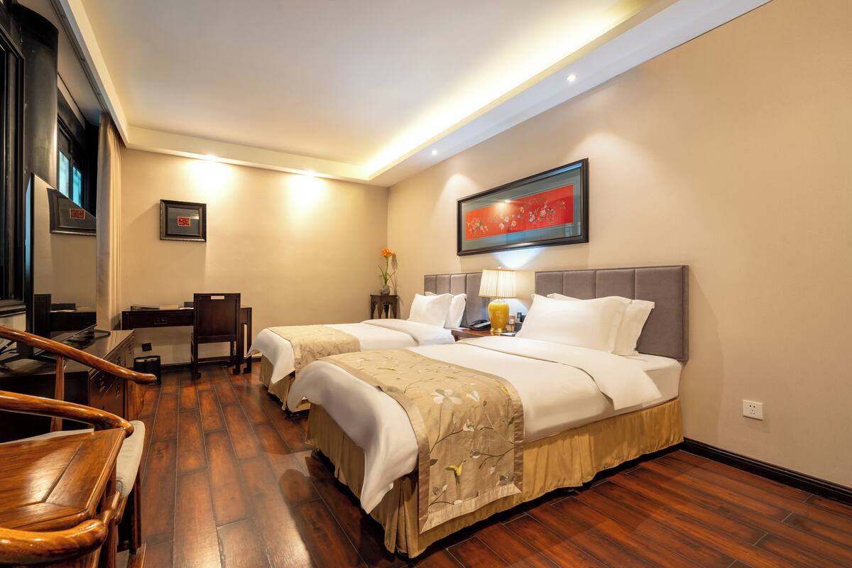 Quarto de hotel com duas camas, uma escrivaninha, uma cadeira e um quadro na parede.