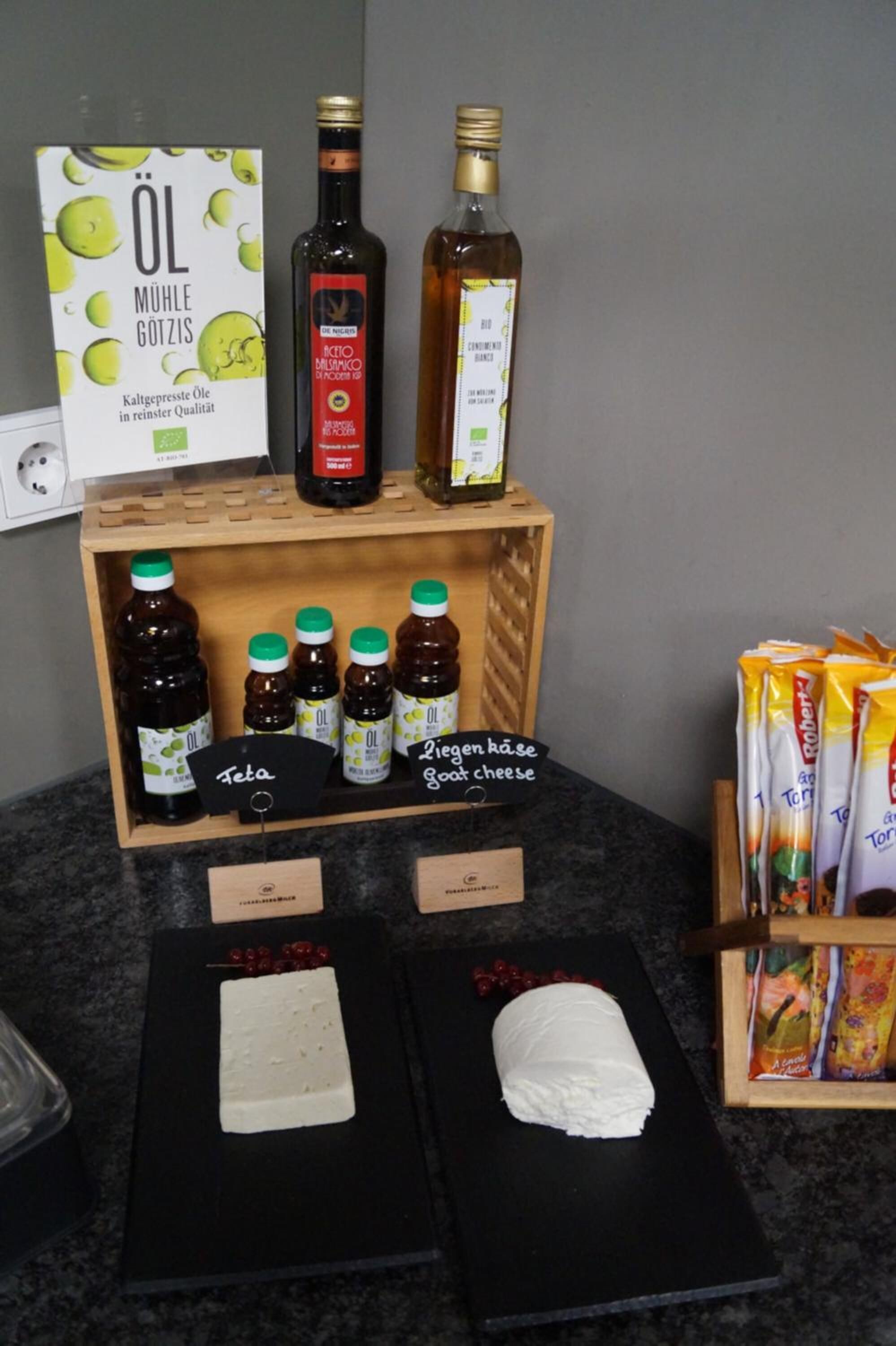 Exposição de alimentos, incluindo garrafas de azeite, uma garrafa de vinho e queijo, tudo com etiquetas.