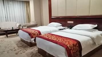 Quarto de hotel com duas camas, um sofá, uma mesa de centro e uma janela grande com cortinas.