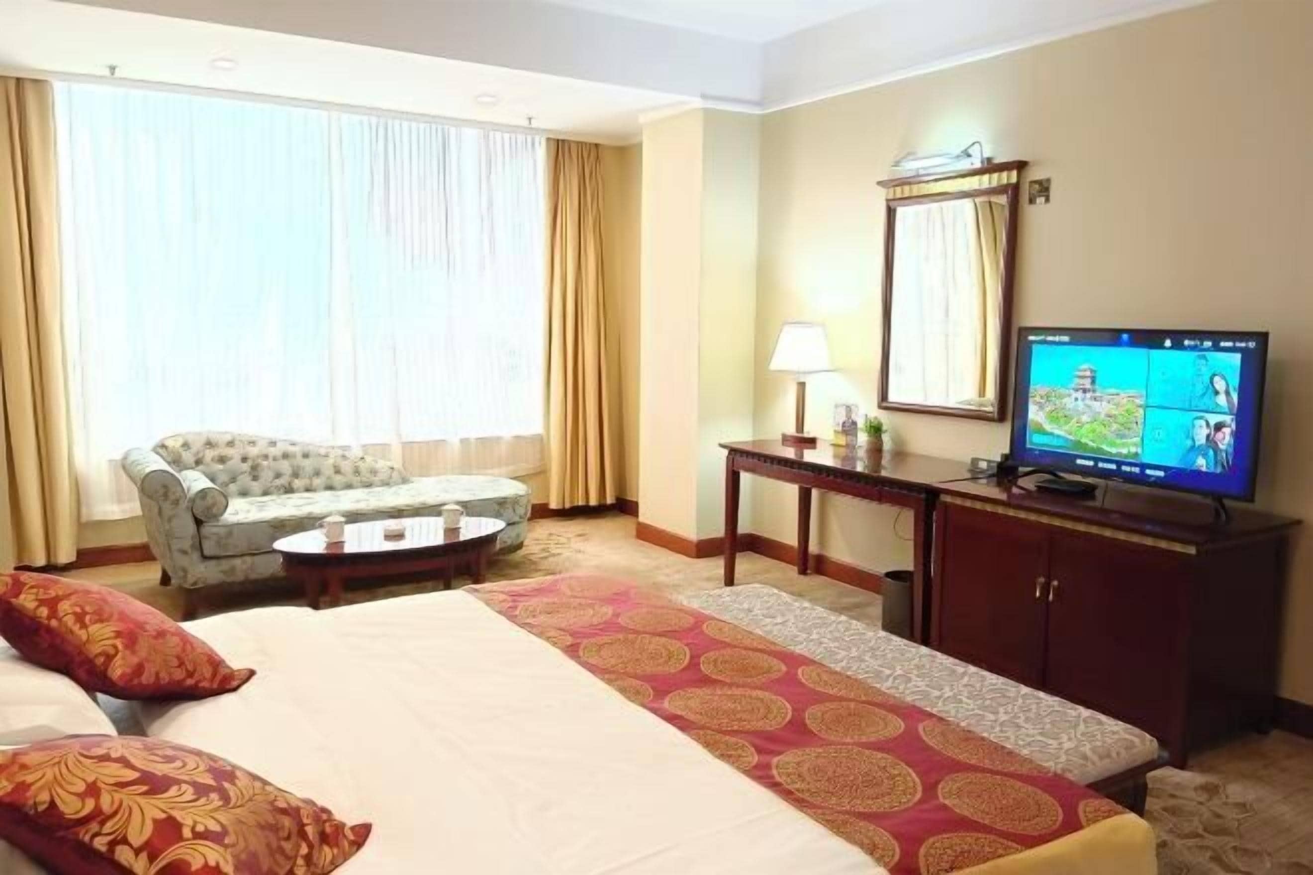 Quarto de hotel com uma cama, sofá, televisão e escrivaninha.