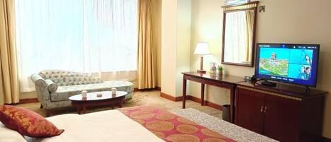 Quarto de hotel com uma cama, sofá, televisão e escrivaninha.